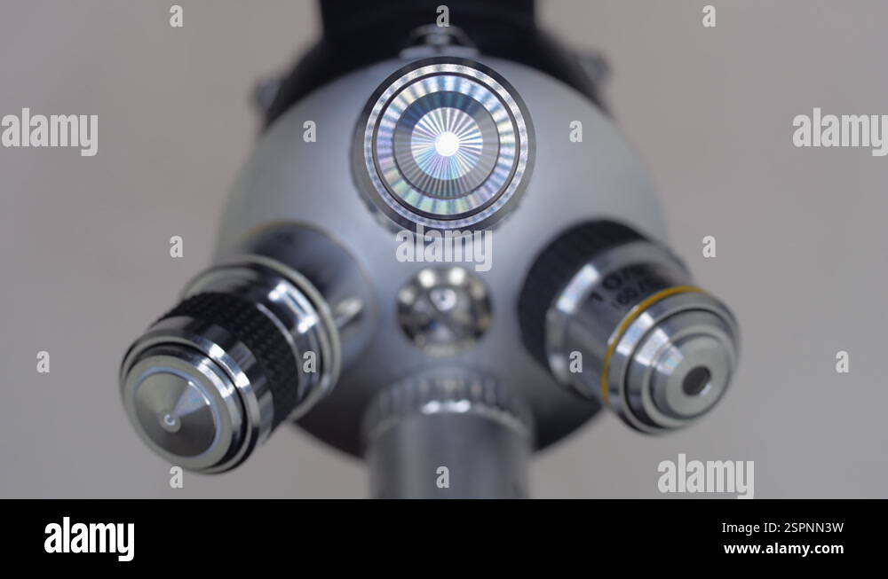 A hand rotates a block of microscope lenses one of them glows brightly ...