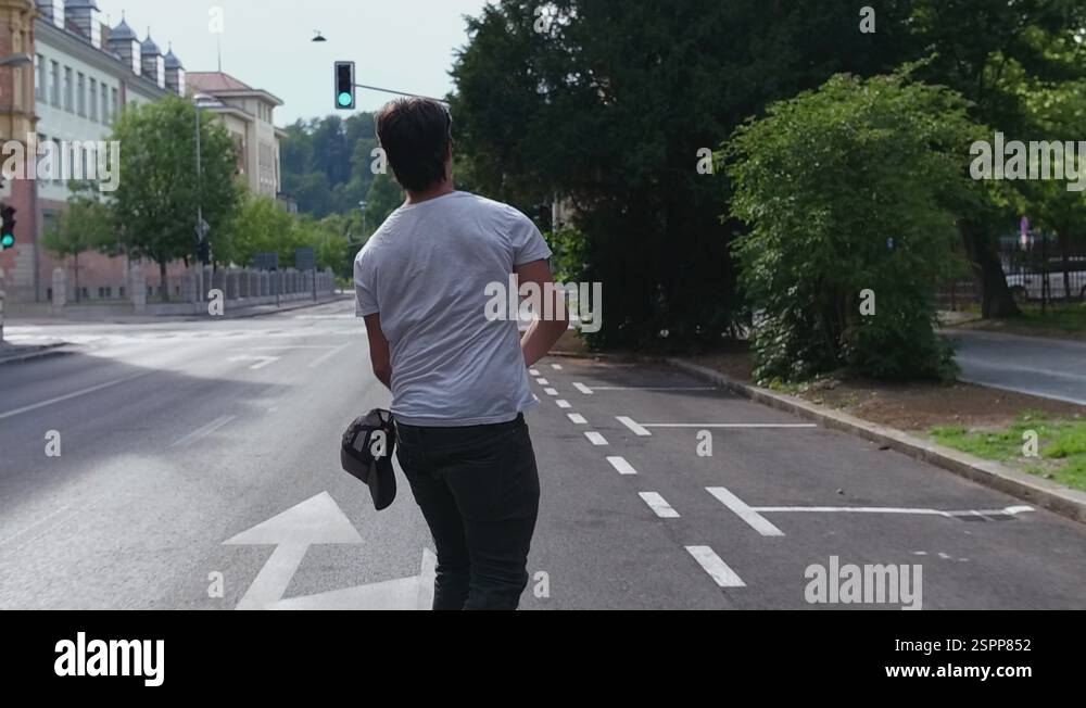 Handheld - Man pushing his skateboard on a city street and looking into ...