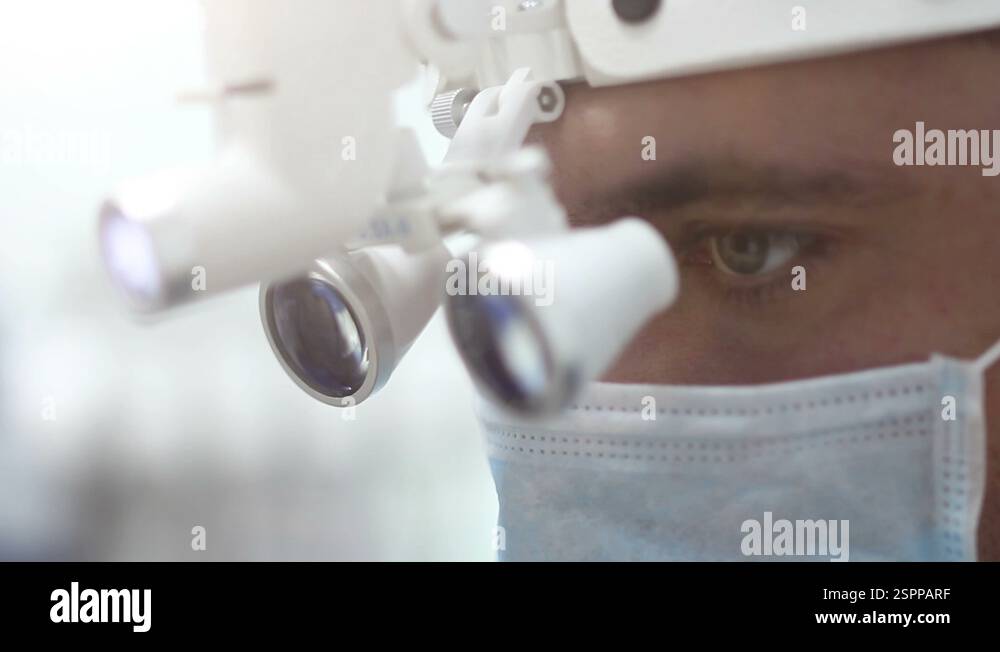 A young doctor with a microscope on his head carries out an operation ...