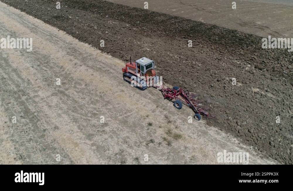 Aerial following tractor on continuous tracks plowing the brown ...