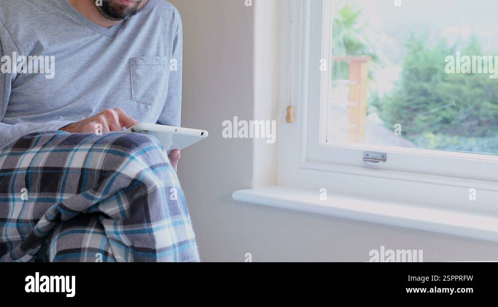 Young man looking out side through window while using tablet 4K 4k ...