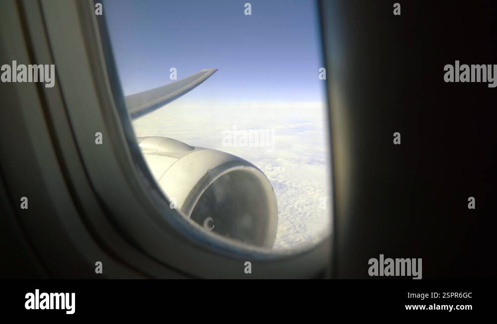 Leaning aircraft passenger window view of airplane turbine above clouds ...