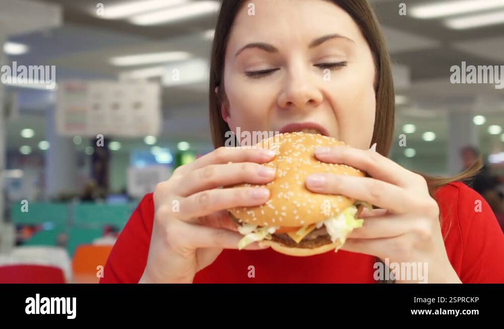 Hungry girl eating hamburger on food court. Woman biting cheeseburger ...