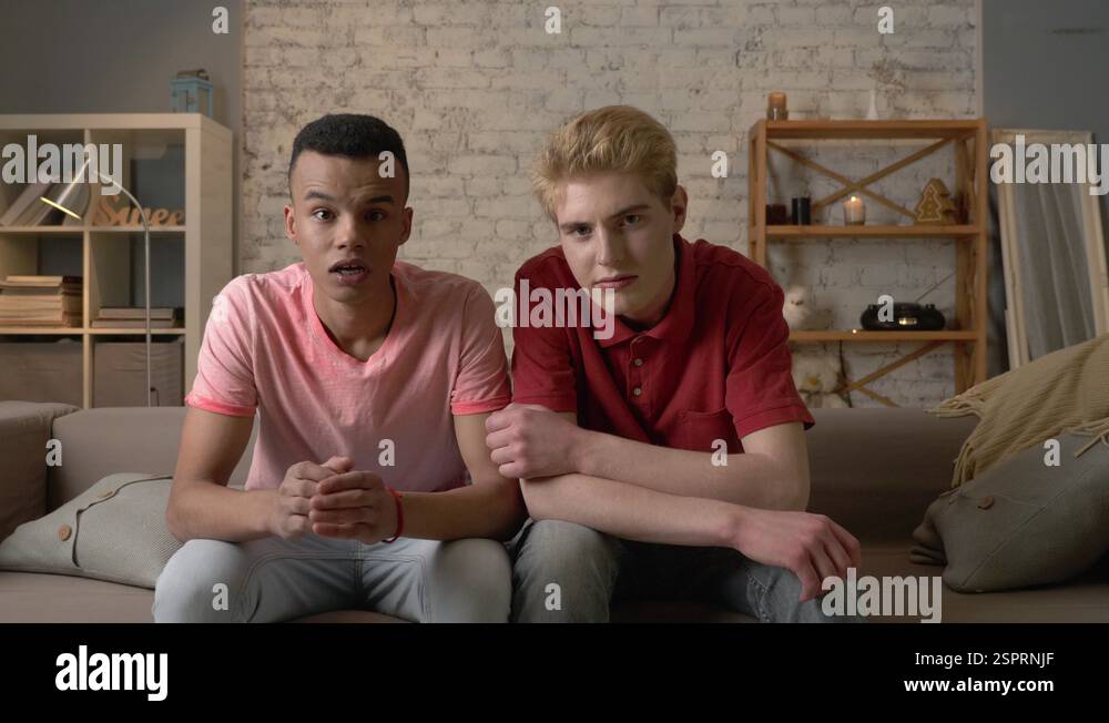 Two gay guys are sitting on the couch and watching TV, emotion of ...