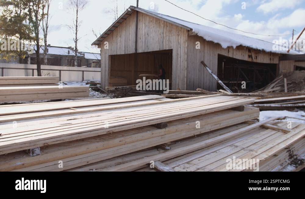 Man working at packs of packed lumber boards stored in yard of sawmill ...