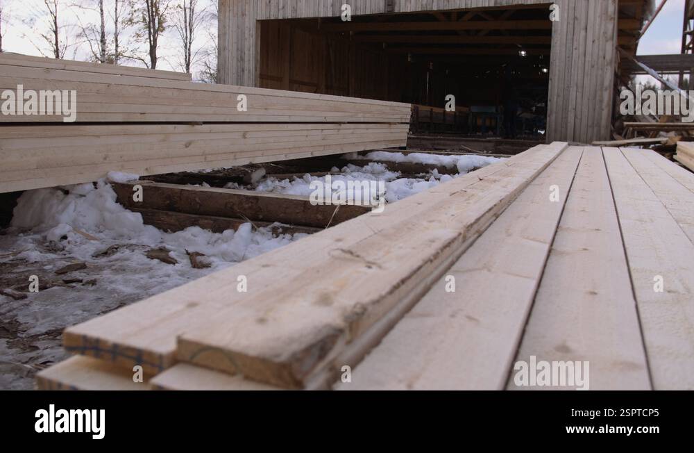Man working at stacks of packed wooden planks stored in yard of sawmill ...