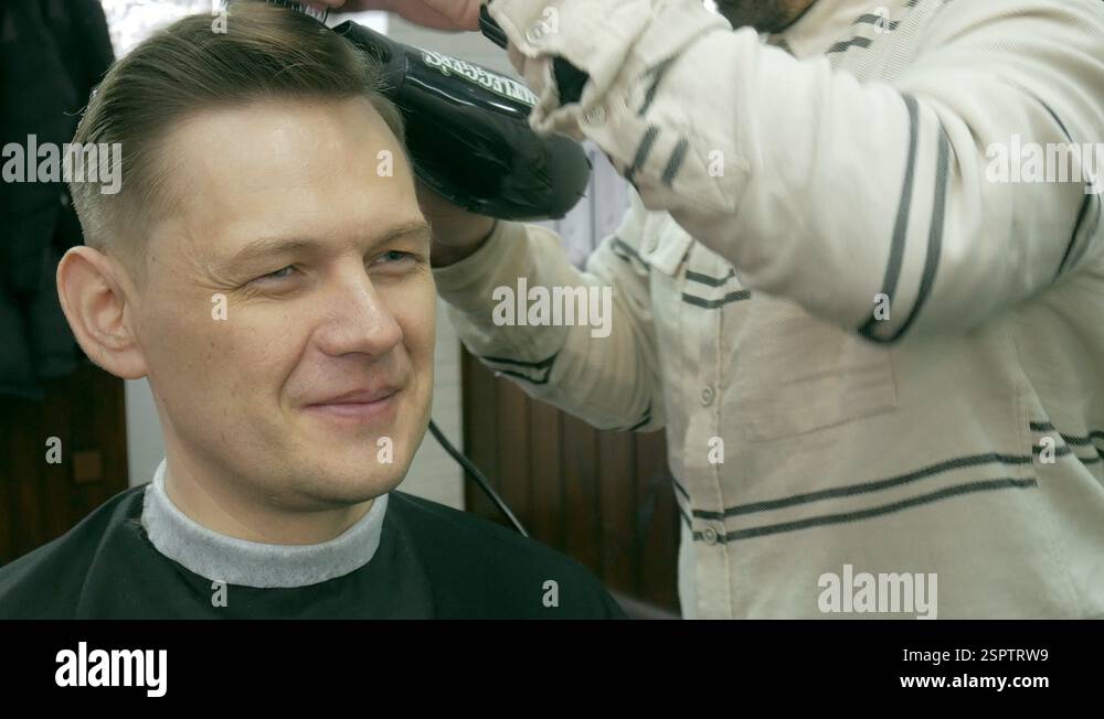 Barber getting groomed at man with hair dryer while sitting in chair at ...
