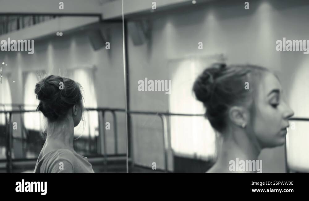 Ballerina in beige sweatsuit and pointe stretches on barre in ballet ...