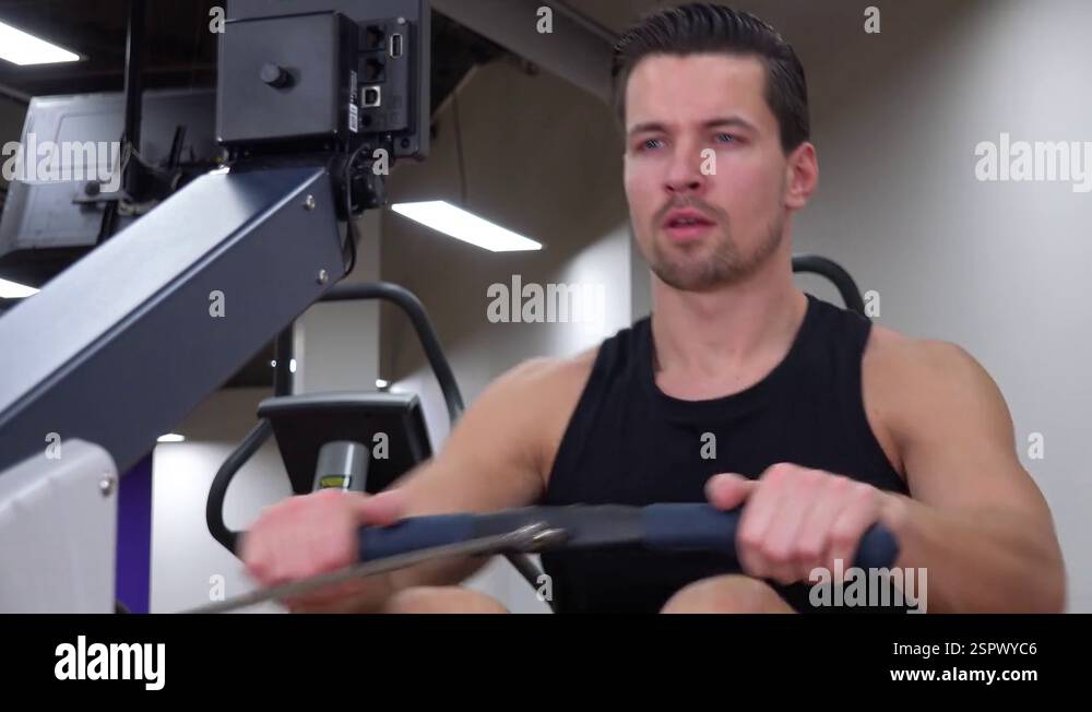 A young fit man trains on a rowing machine in a gym - closeup Stock ...