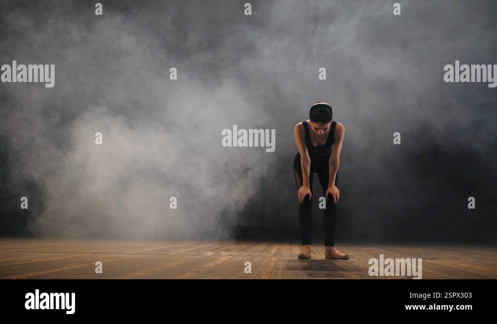 Young beautiful tired ballerina in black suit stands on stage with ...
