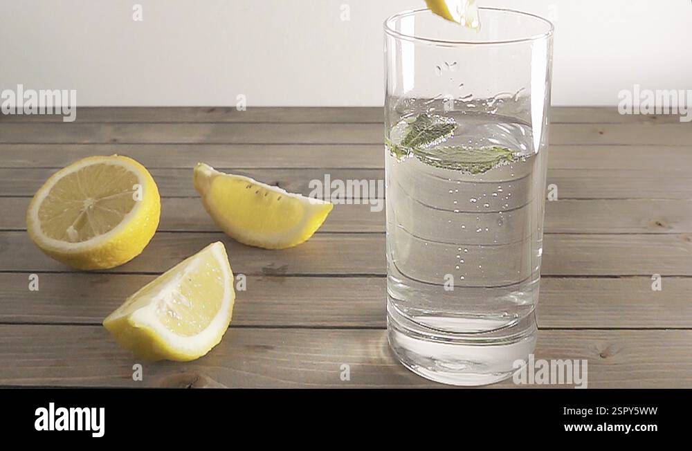 Piece of lemon falling down into transparent glass of mineral water ...