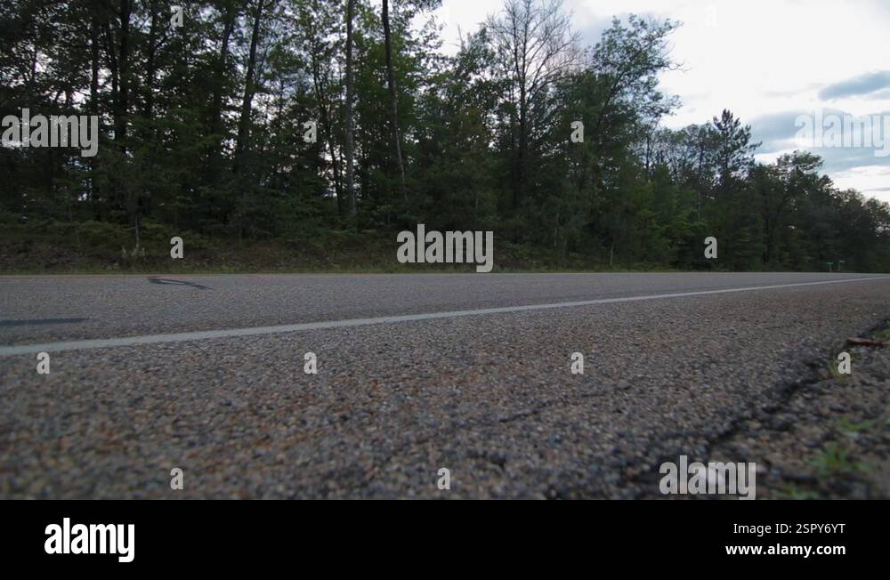 Brown car drives past on Michigan country paved road during an overcast ...
