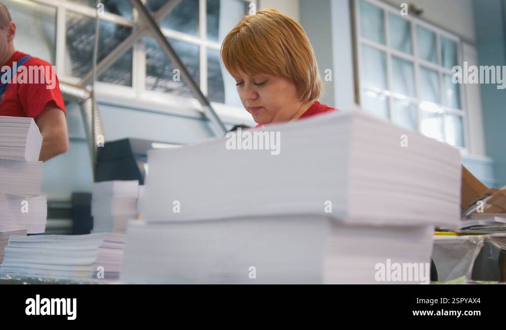 Paper stack in front of woman worker sorting a printed edition in the ...