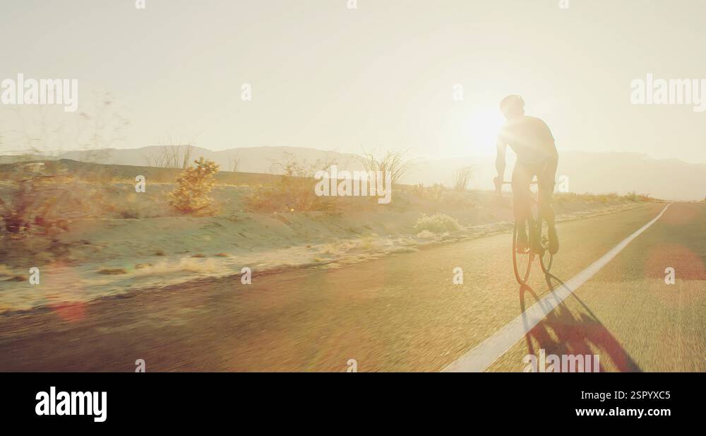 Young man cycling on road bike outside on desert road at sunset with ...