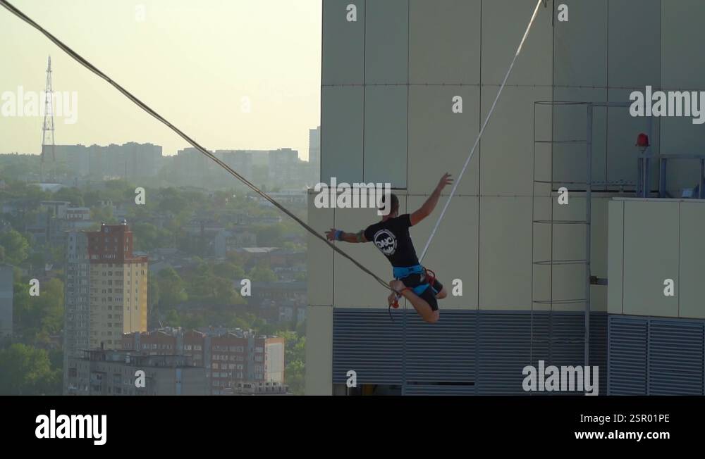 A man sits on a tight rope between skyscrapers and tries to keep his ...