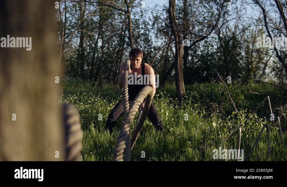 Young fit man practicing in the park. He uses crossfit ropes for ...