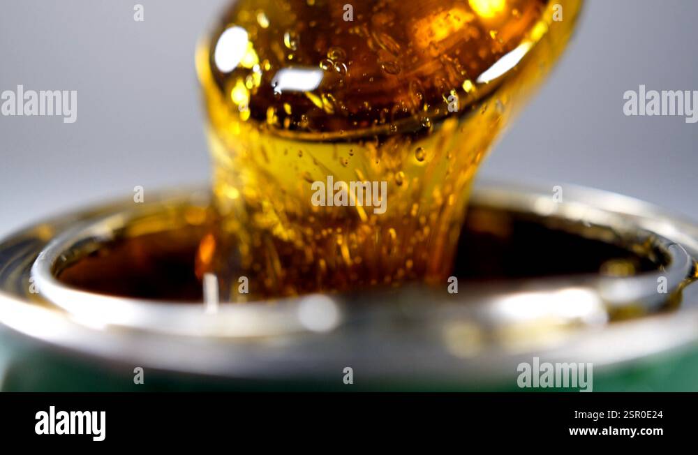 golden syrup pouring into a metal container using a spoon against a ...