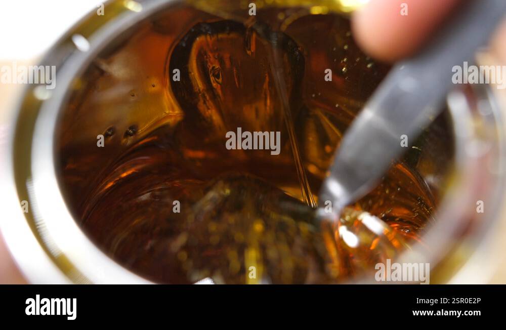 golden syrup pouring into a metal container, with a serving spoon, a ...
