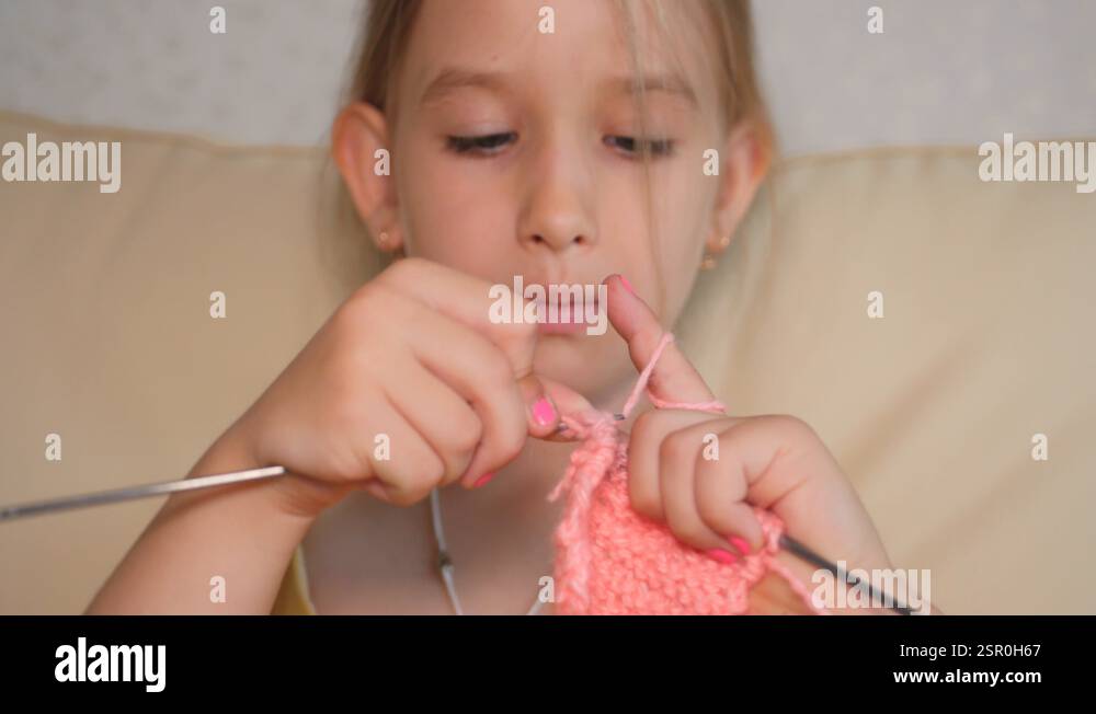Little girl sitting on couch and knitting wool scarf. Young girl using ...
