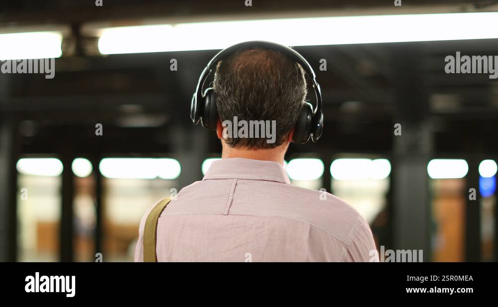 Behind back shot of man listening to music with over the ear headphones ...