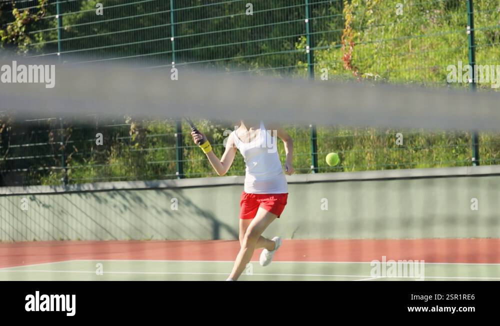 Good-looking young woman hits the tennis ball, smiles to her opponent ...