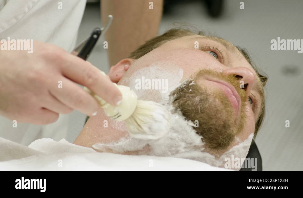 Barber putting shaving cream on client before shaving his beard in ...