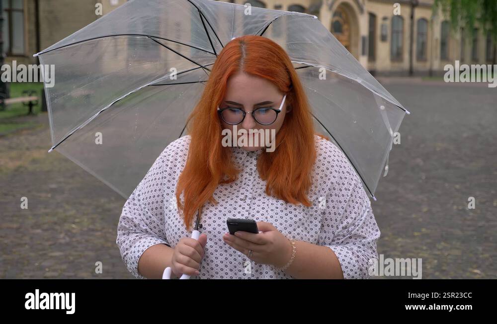 Fat ginger girl with glasses is typing message on smartphone in park in ...