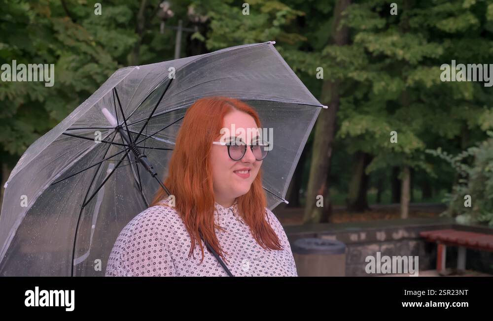 Fat ginger girl with glasses is crossing on road in park in rainy ...