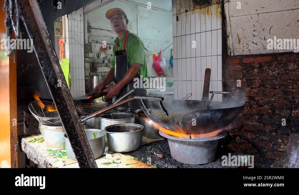Guy is cooking food in a street restaurant of Xian Urban Village slums ...