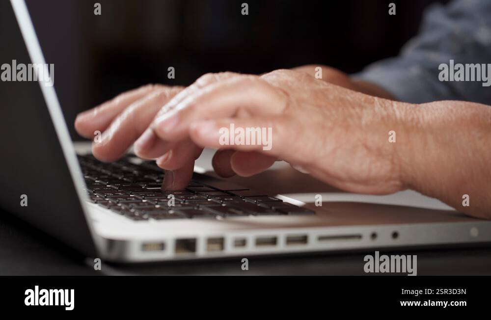 Grandmother works behind laptop, typing on keyboard with her old hands ...