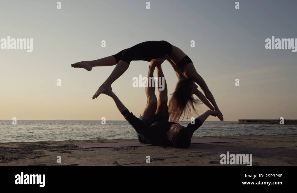 Silhouettes of fit young couple doing acro-yoga at sea beach. Man lying ...
