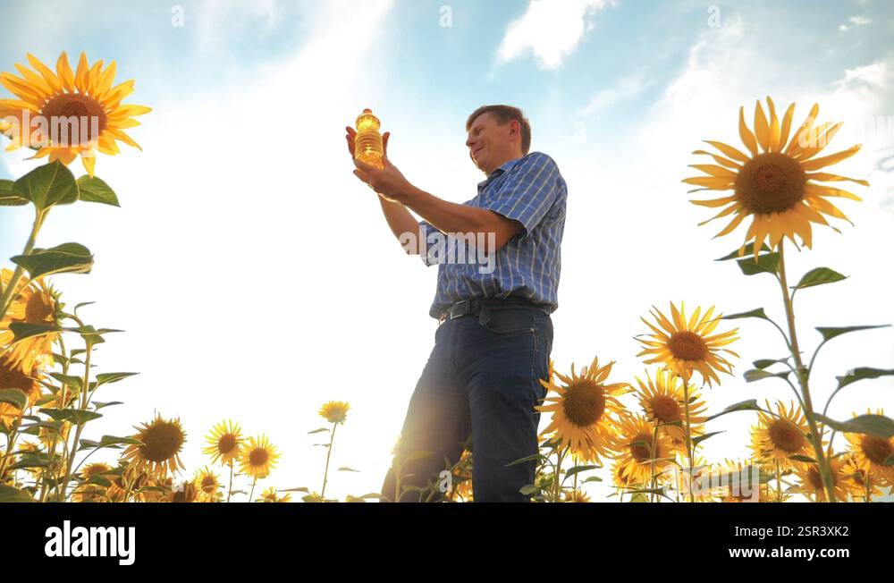 old man farmer holding in hand a plastic bottle sunflower oil stands in ...