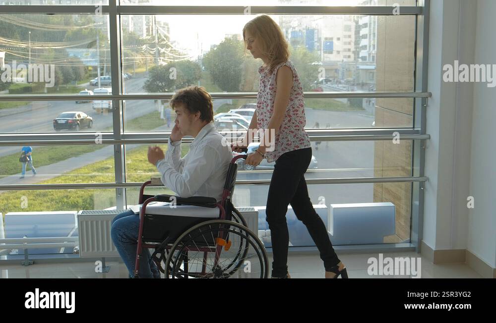 Business woman wheeling a wheelchair with a disabled businessman on a ...