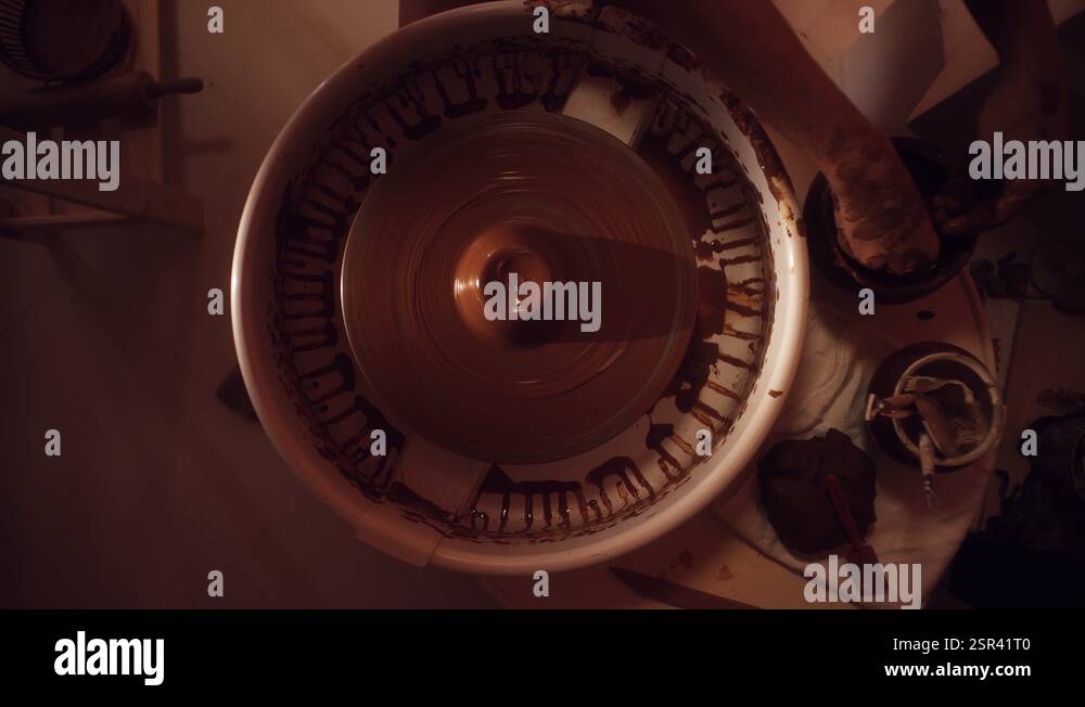 Top view of rotating potter's wheel with hands shaping small brown clay ...