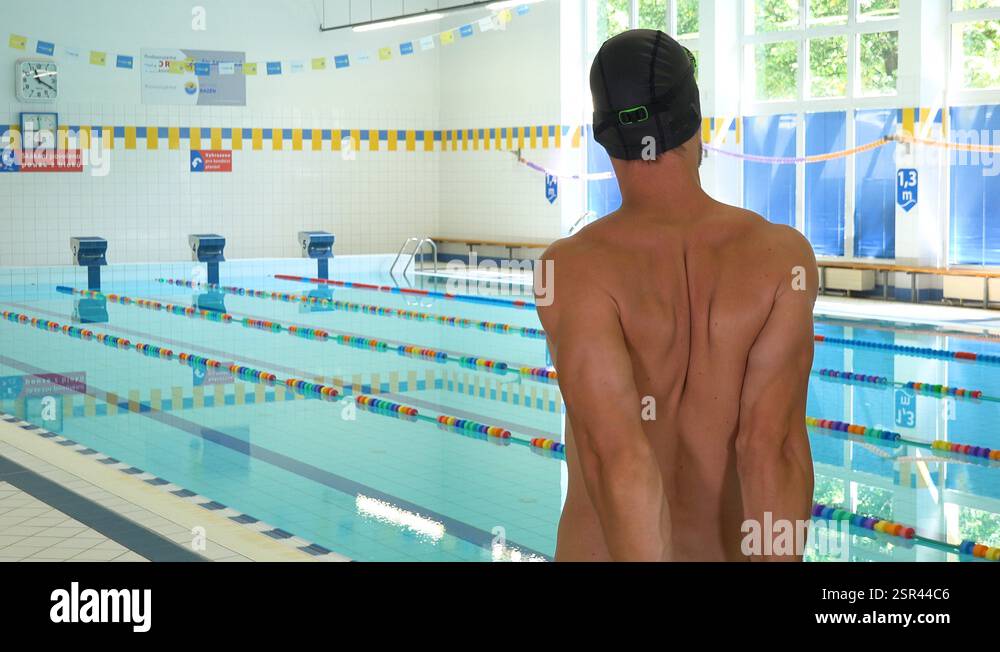 A professional swimmer stretches at an indoor pool with his back to the ...