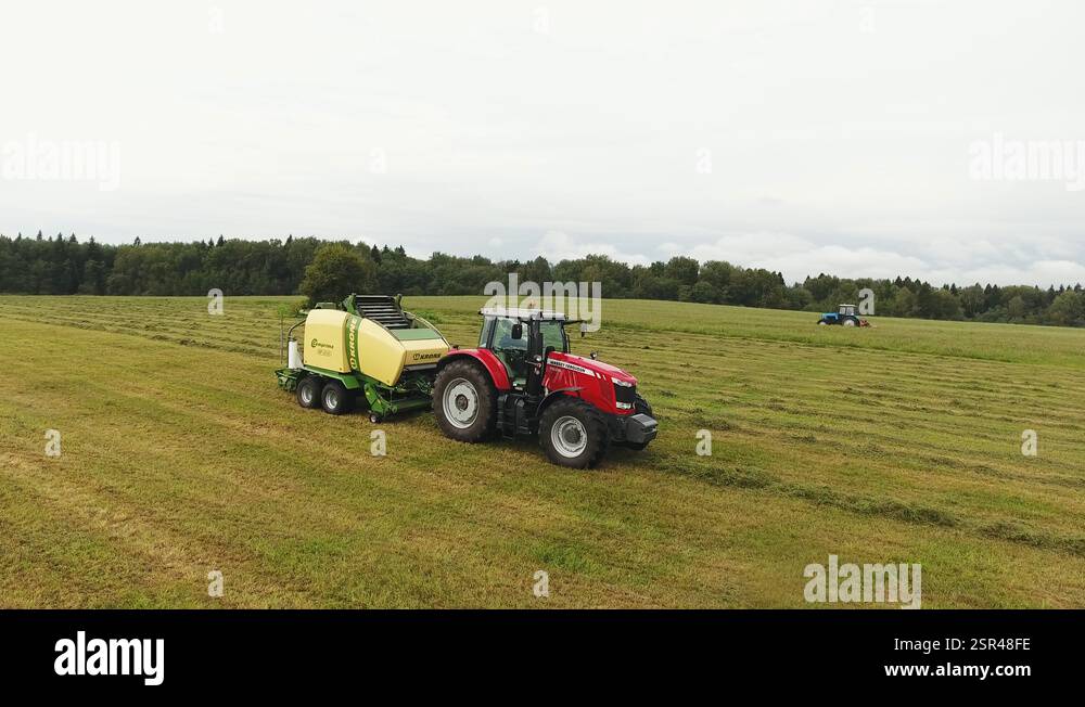On large field yellow hay baler attached to big red tractor makes round ...