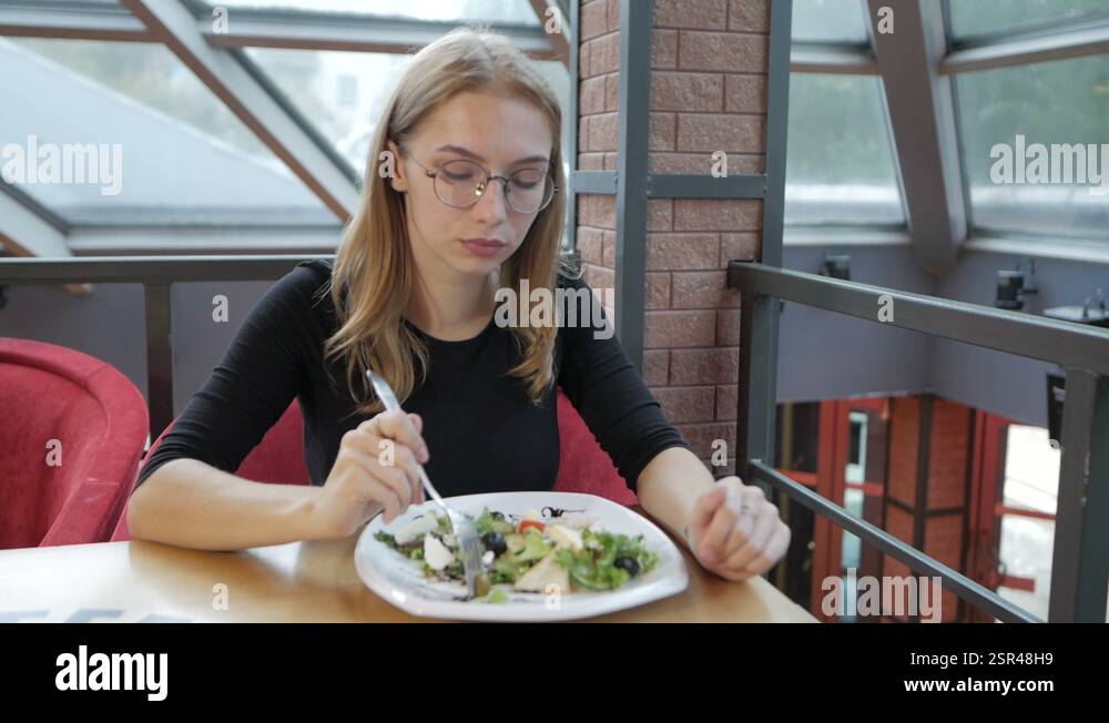 A young girl with glasses sitting in a cafe eating a Caesar salad Stock ...
