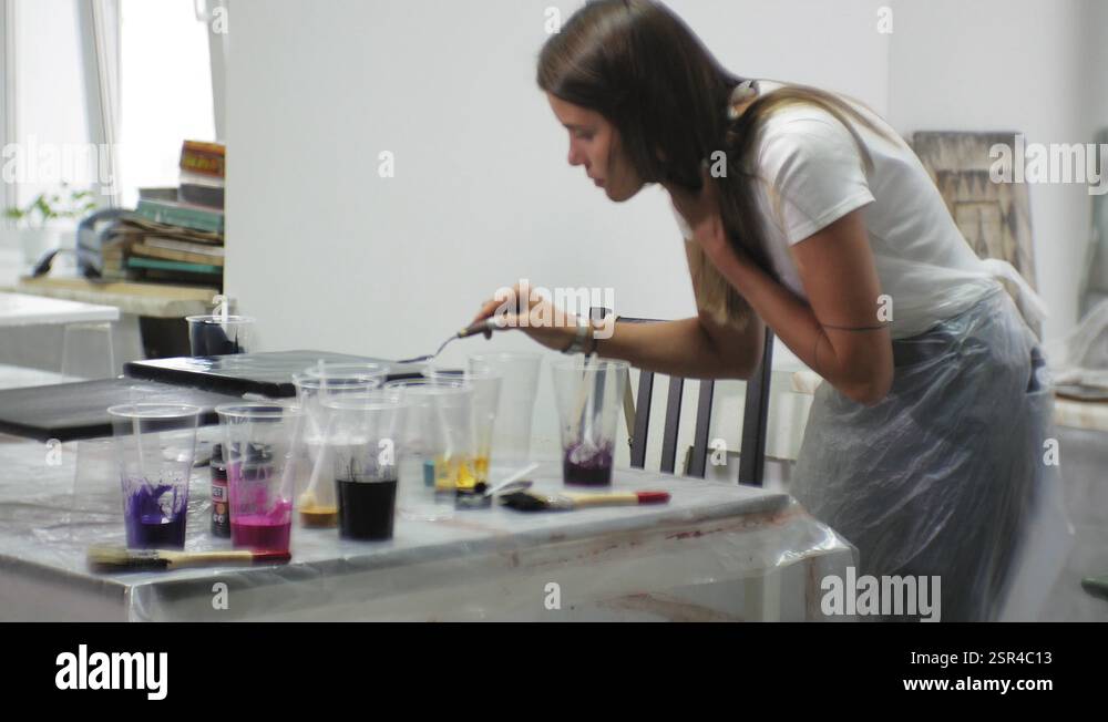 women in an art studio mix paints and draw on canvas in fluid art ...