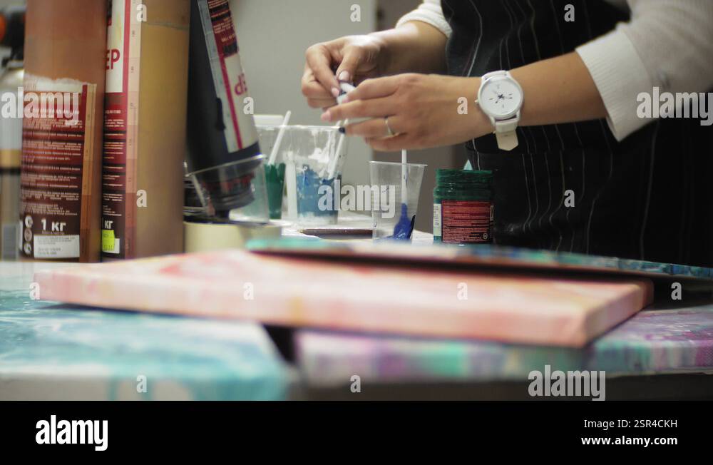 women in an art studio mix paints and draw on canvas in fluid art ...