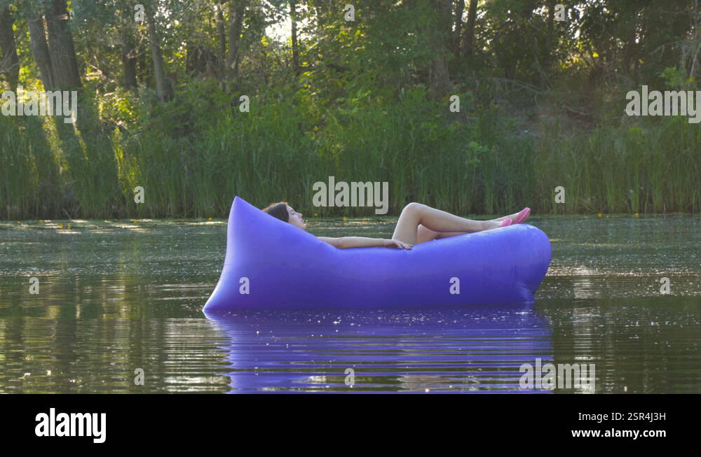 A young woman lying on an airbed takes sunbathing and sails along the ...