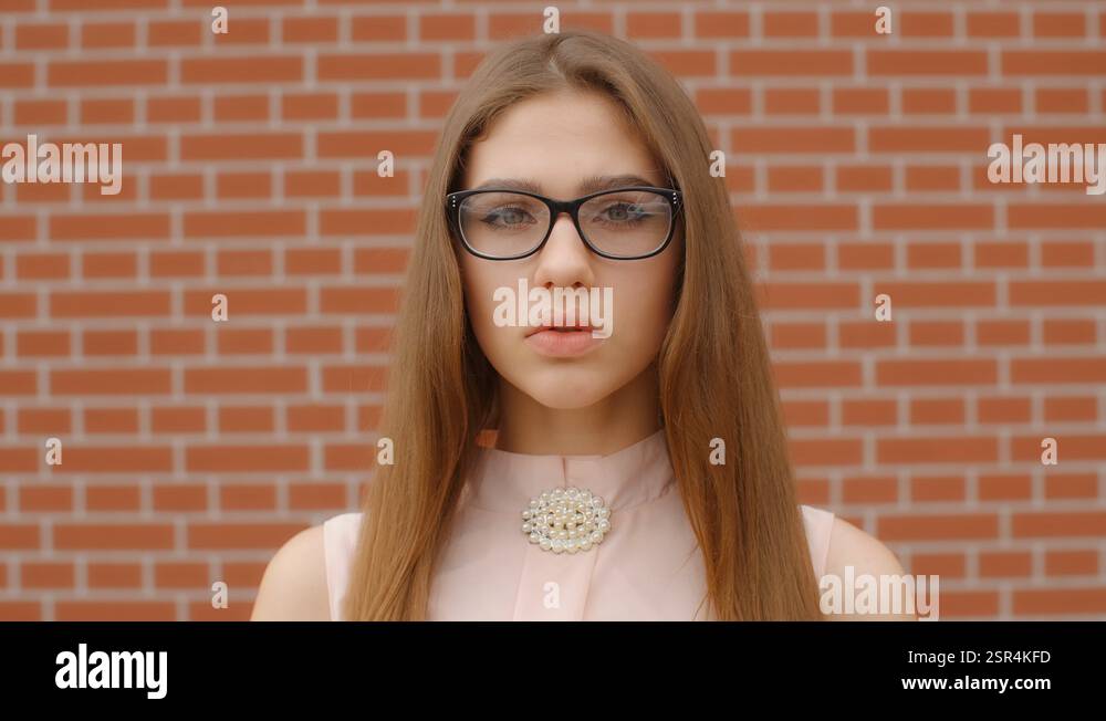 Upset girl student in glasses saying no to the camera against a brick ...