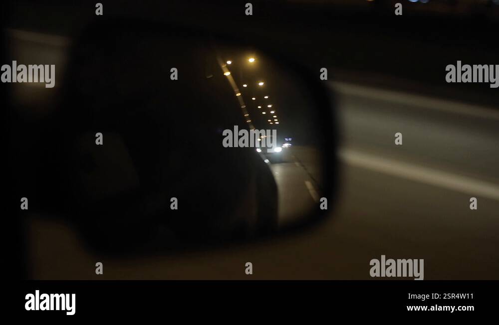 Reflection of a moving vehicle in a wing mirror. Going by car at night ...