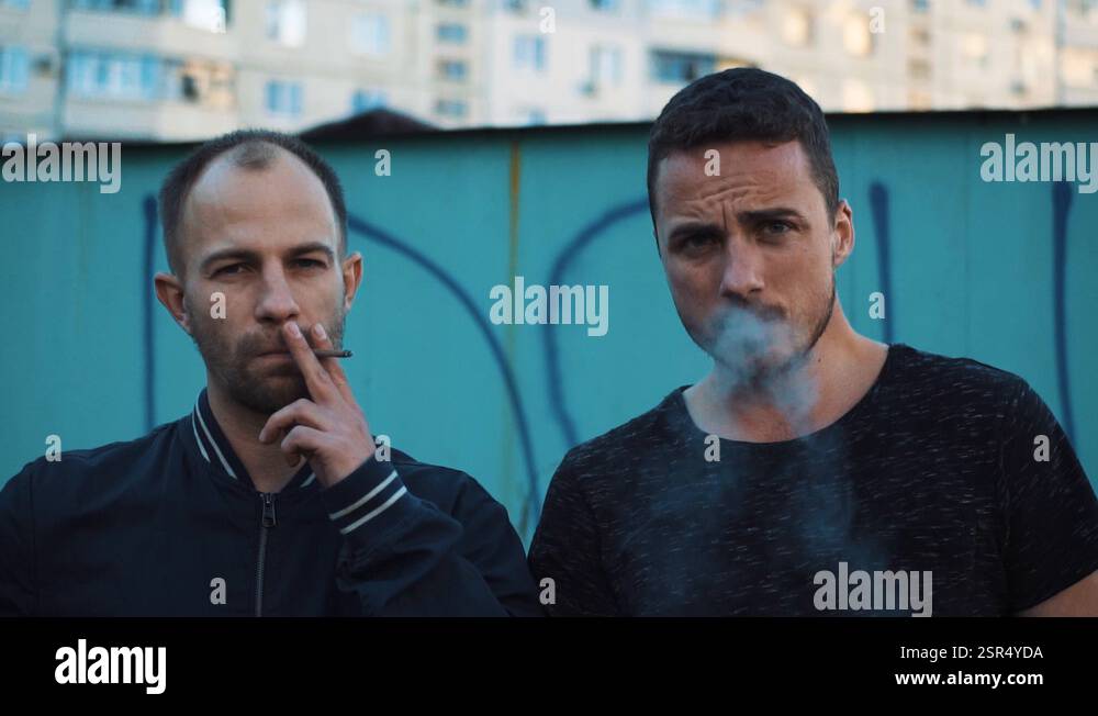 Two men smoke cigarettes in the ghetto and look into the camera Stock ...