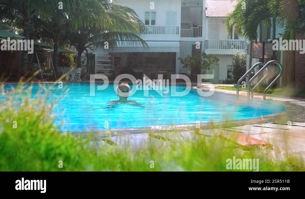 girl swims across hotel swimming pool to barrier among palms Stock ...