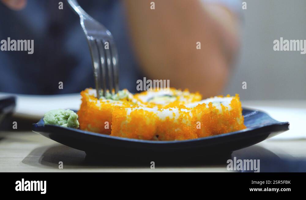 Close-upman's hands put wasabi on the roll with a fork and dip the roll ...