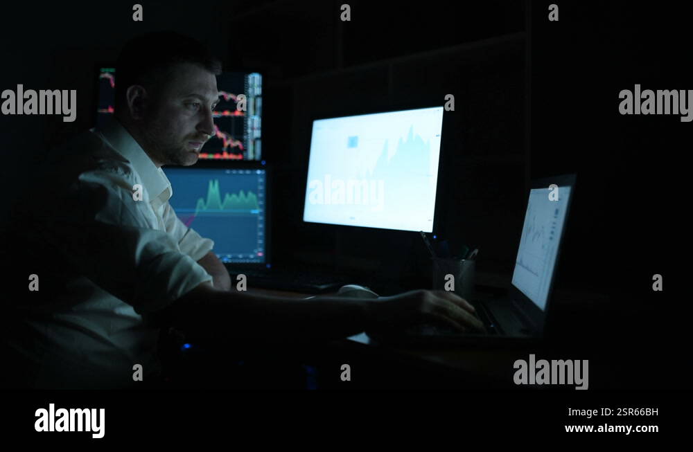 Stockbroker in white shirt is working in a dark monitoring room with ...