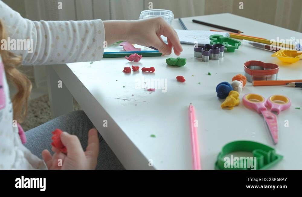 a little girl plays with plasticine, separates into small pieces, on ...