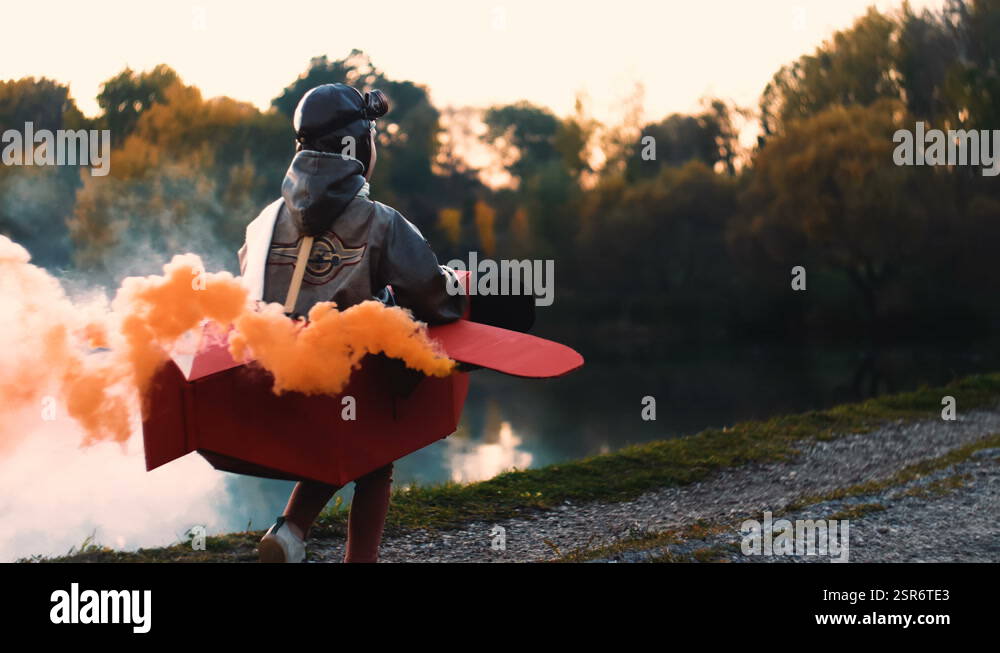 Camera follows happy little aviator boy running along sunset lake in ...
