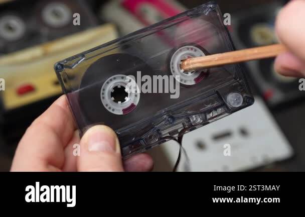 Rewinding magnetic tape in a cassette manually with a pencil, close up. Old methods of rewinding ...