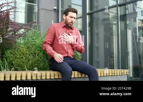 Man in red shirt shows signs of distress as he clutches chest ...
